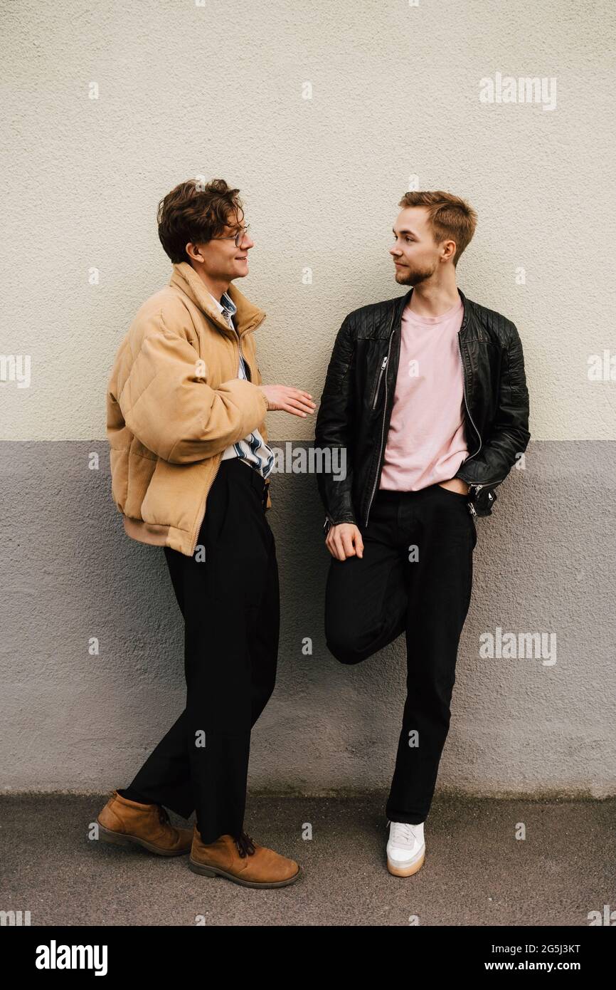 Male friends talking with each other while leaning on beige wall Stock ...