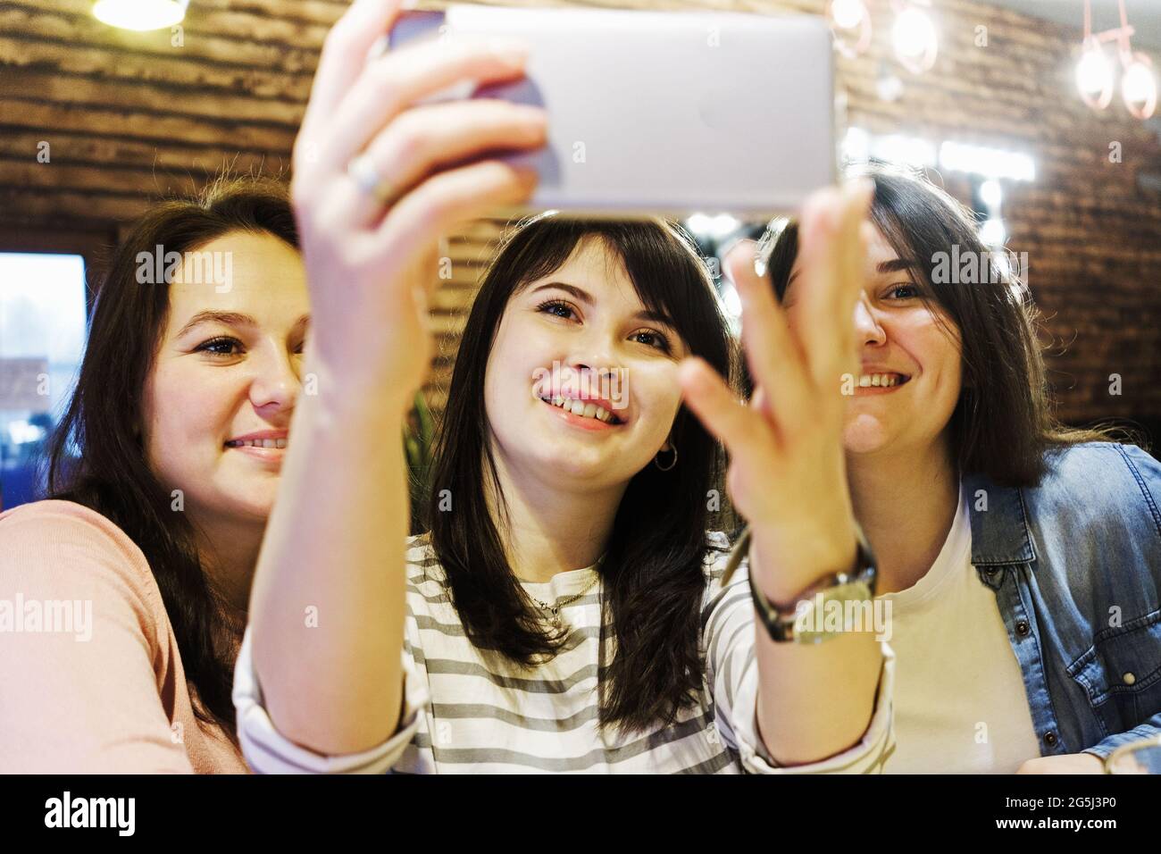 Three girlfriends in a cafe having fun and taking selfies - Cheerful ...