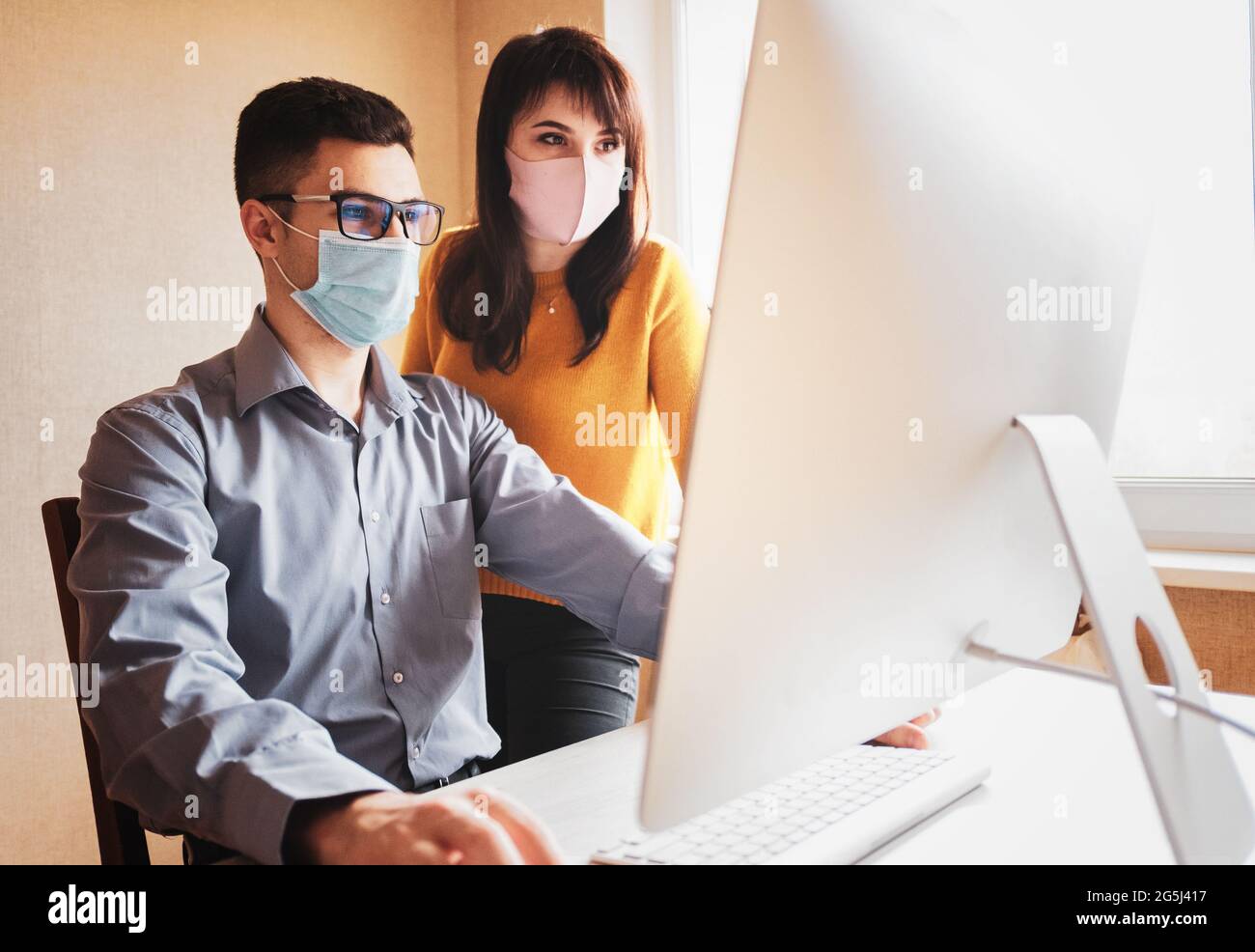 Two colleagues in the office are working on a new project with masks on ...