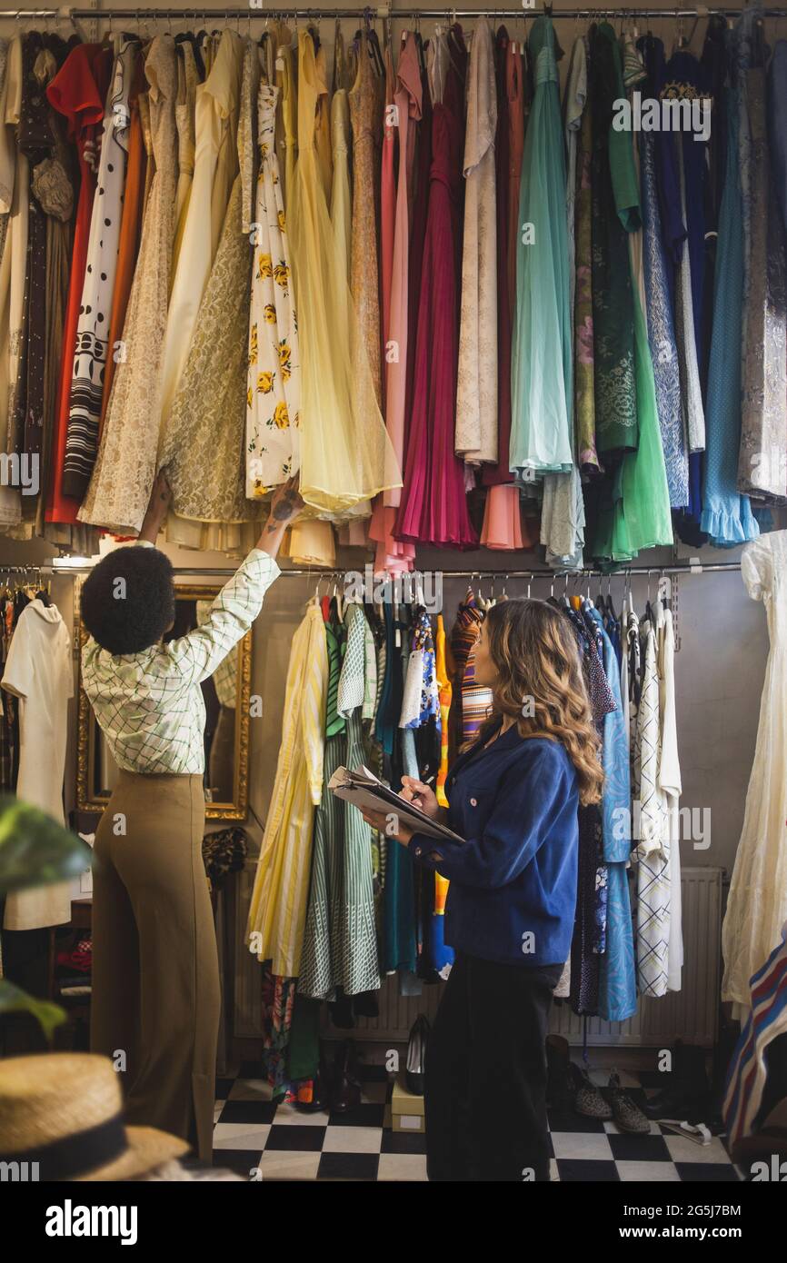 Rear view of owner arranging clothes while female entrepreneur making ...