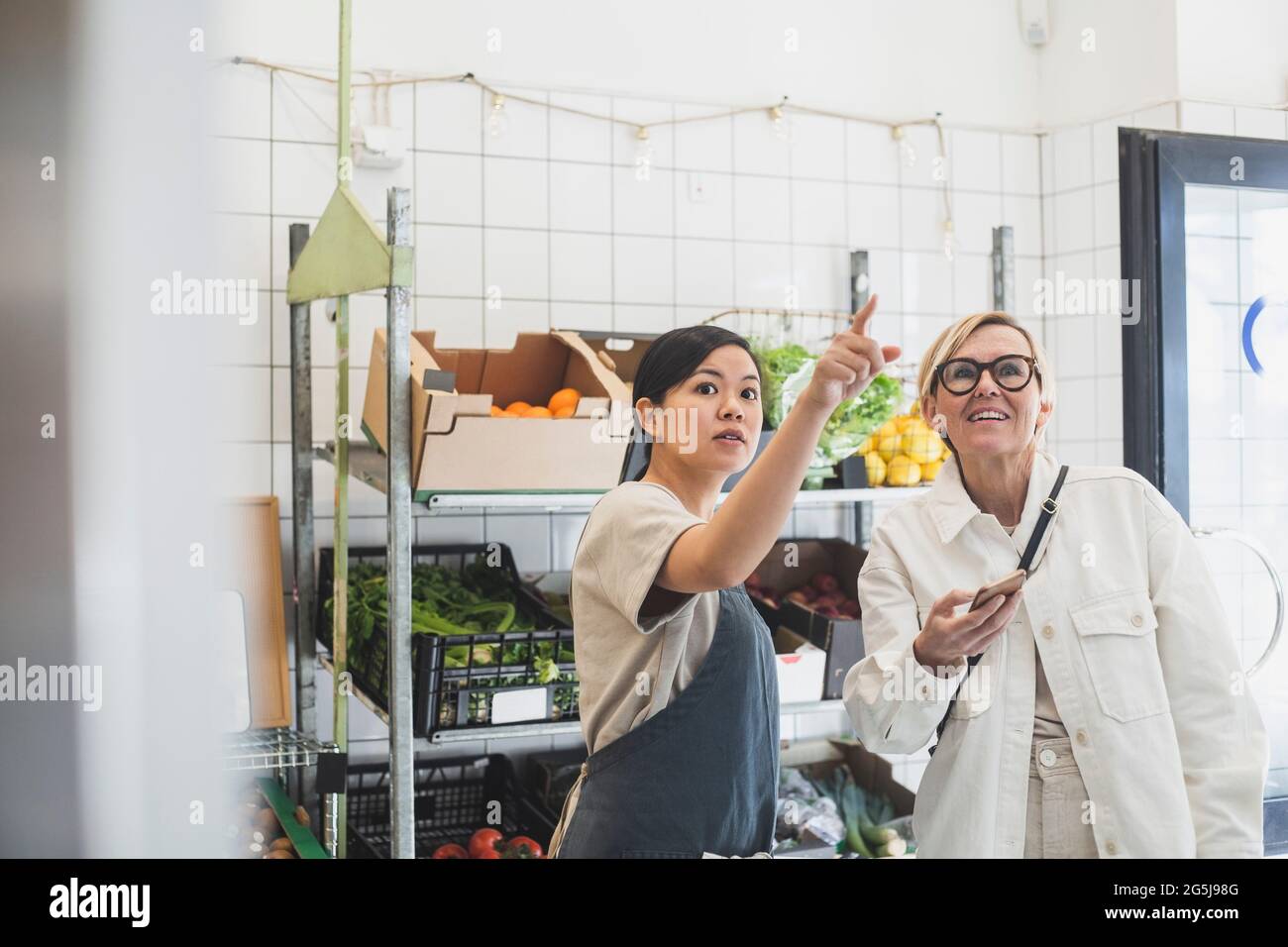 Female owner pointing while talking with female customer in store Stock ...