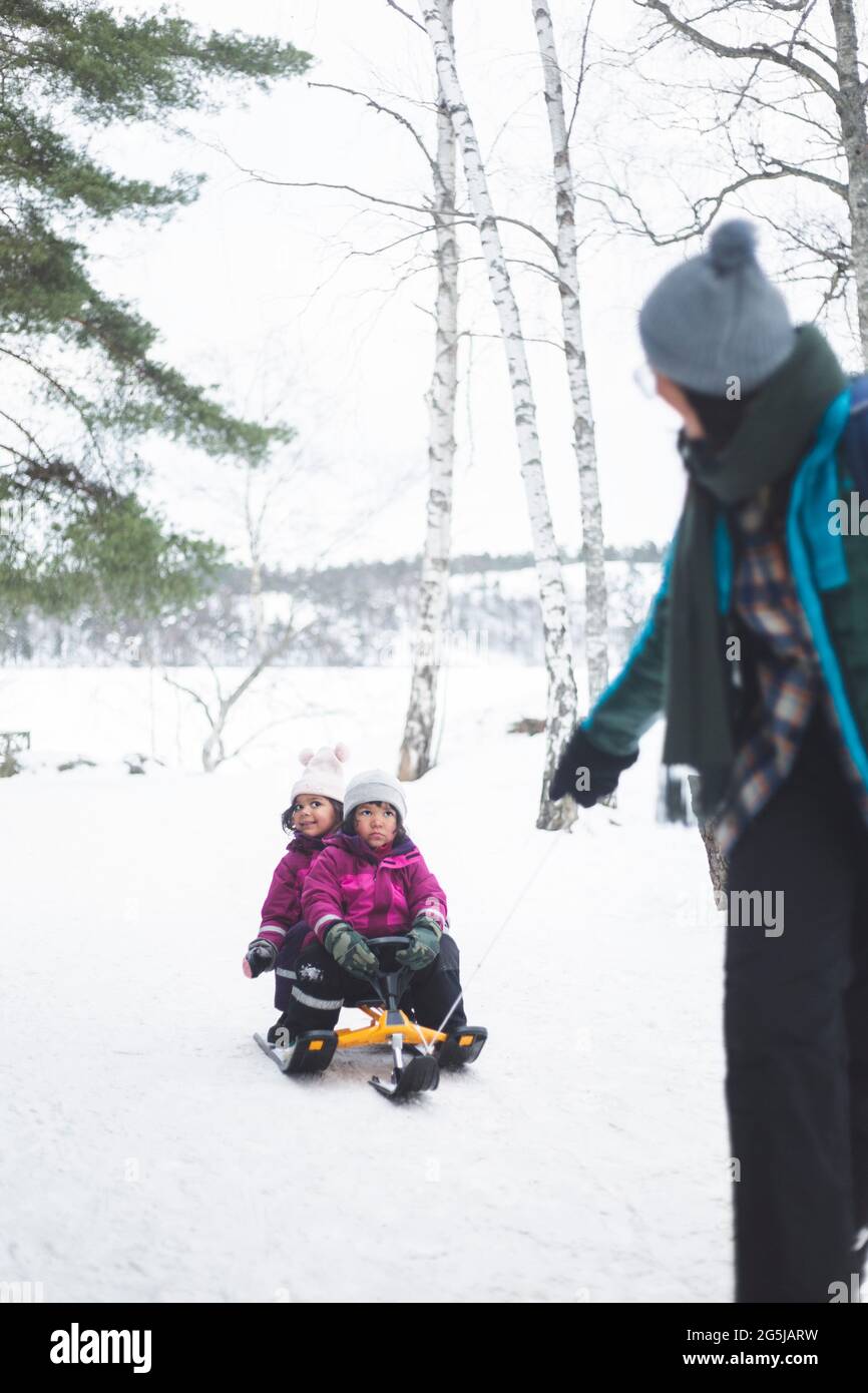 Woman pulling girls sitting on sled during winter Stock Photo - Alamy