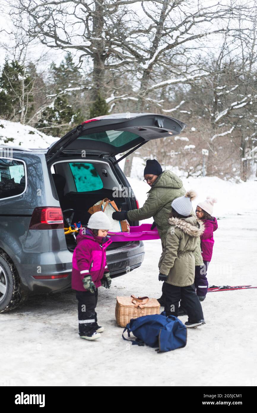 Mother and daughters unloading luggage from car trunk during winter ...