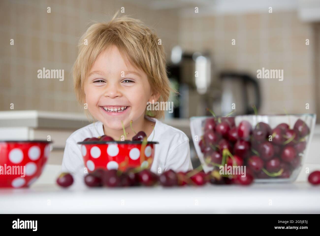 Cute blond child, toddler boy, eating cherries at home, having fun ...