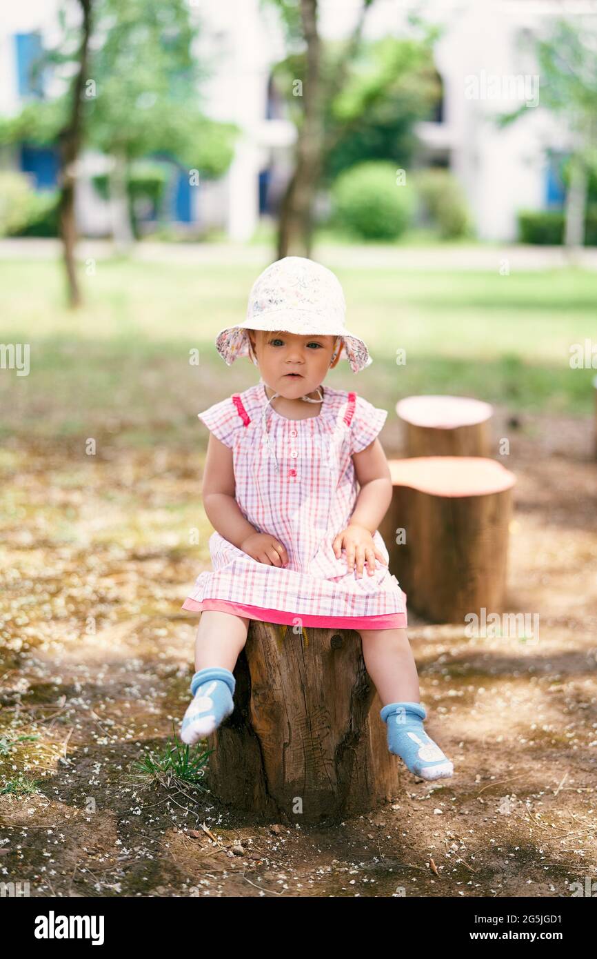 Little girl in a hat sits on a tree stump in the yard Stock Photo - Alamy
