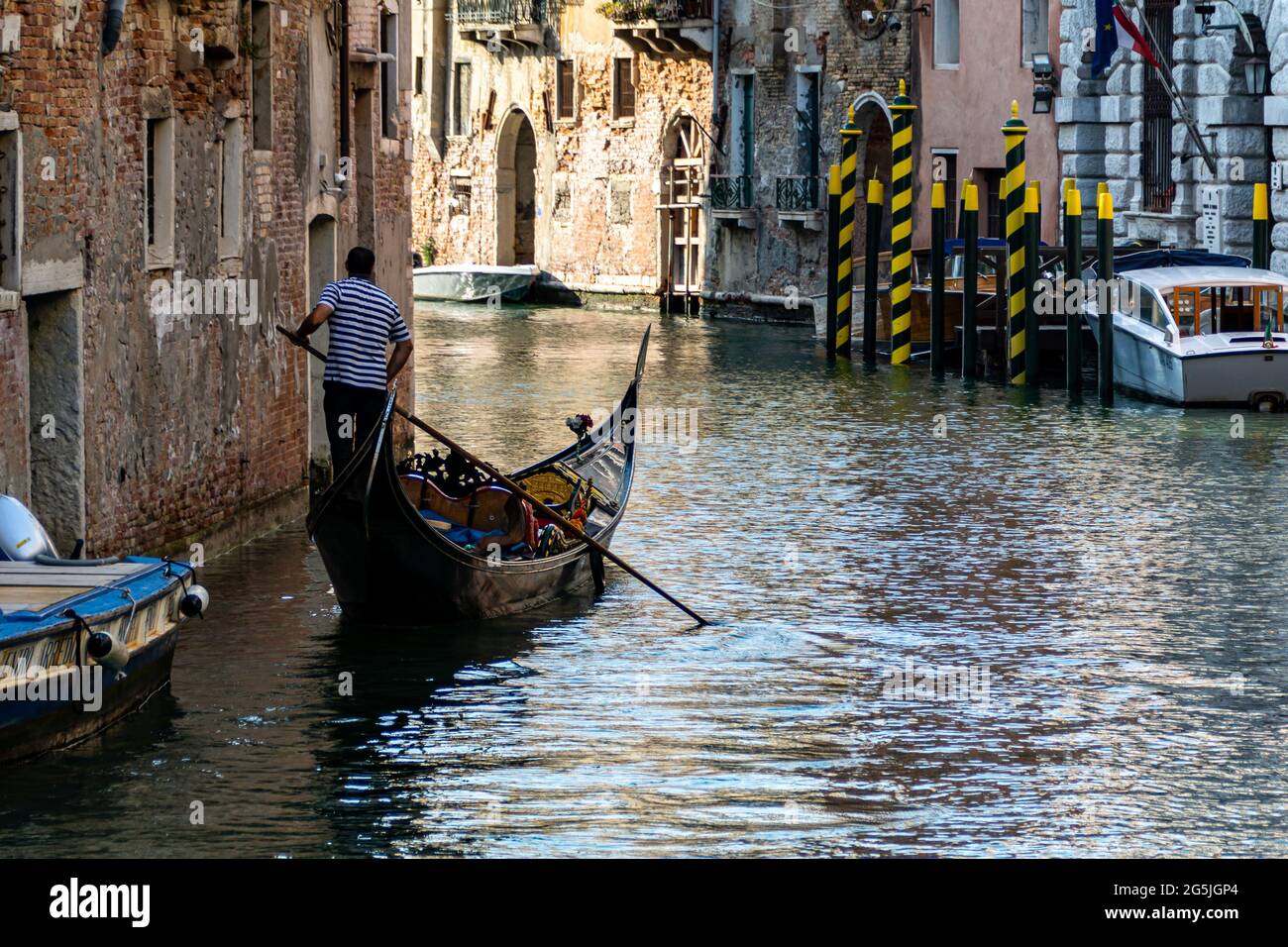 Venetian gondolier, rowing a traditional gondola through the green ...