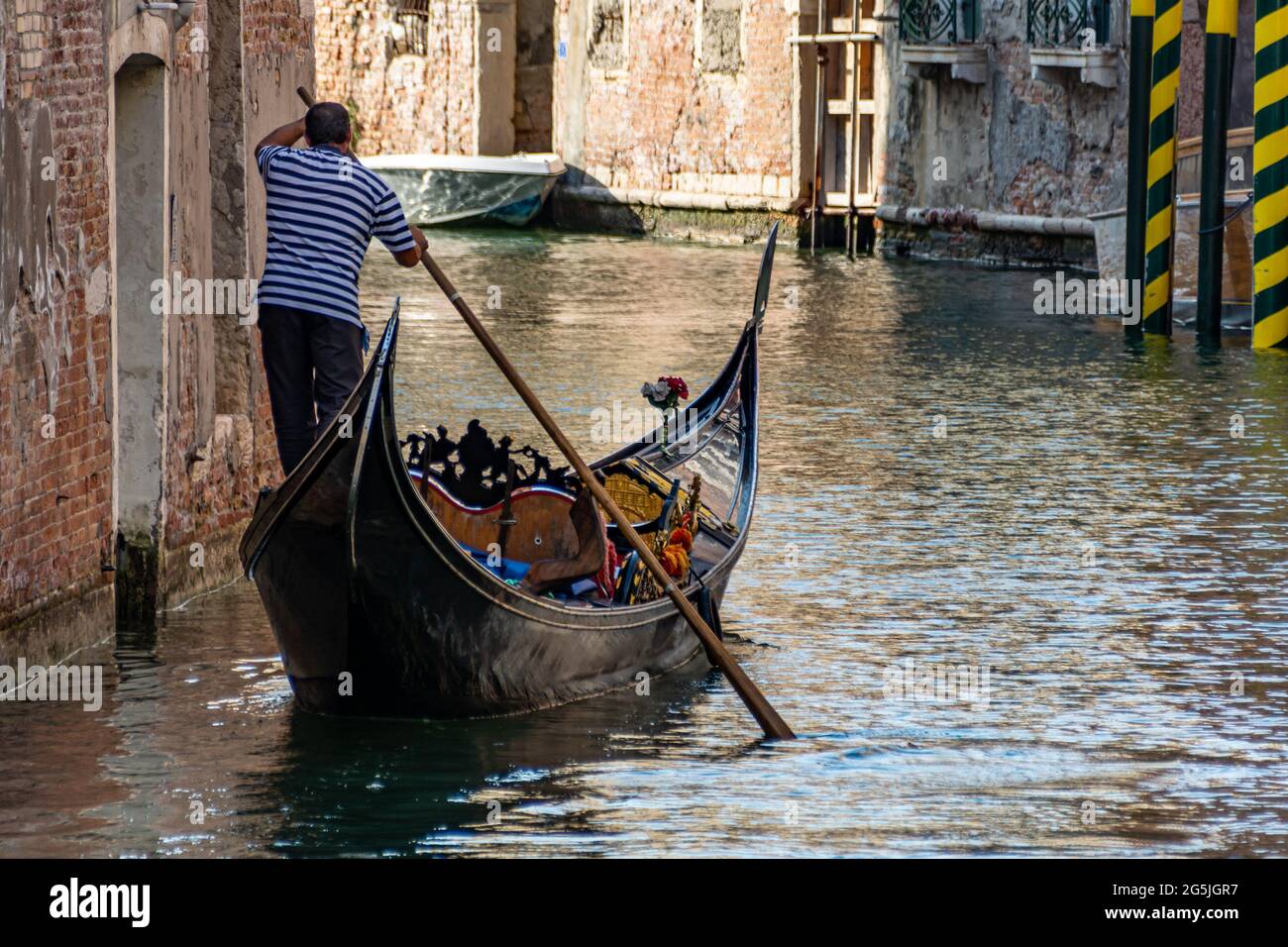 Venetian gondolier, rowing a traditional gondola through the green ...