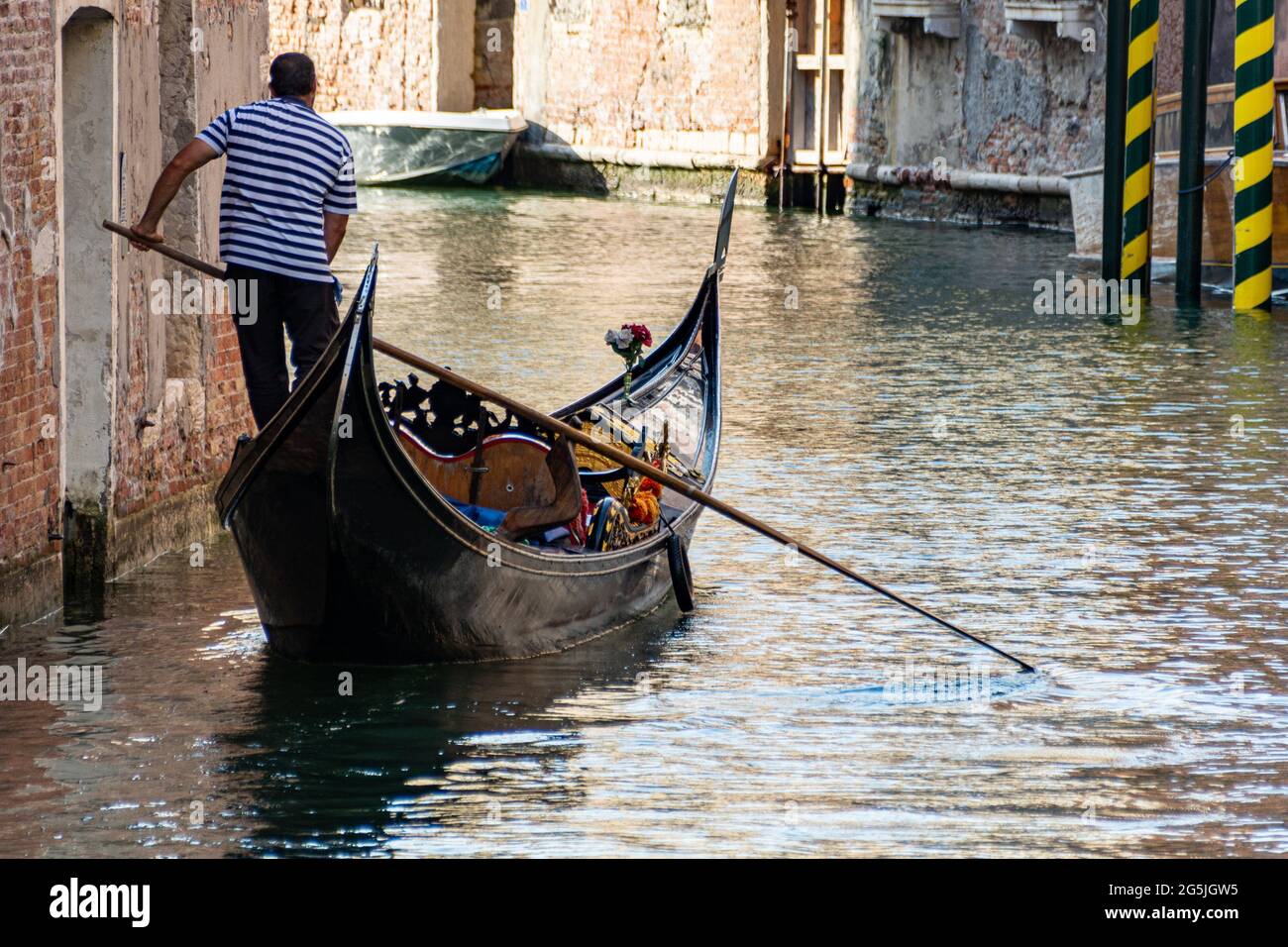 Venetian gondolier, rowing a traditional gondola through the green ...