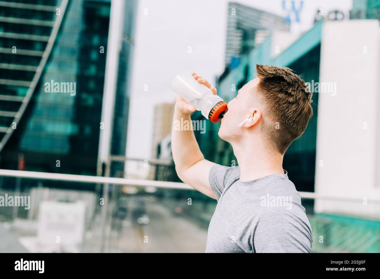 Tired Young man runner drinking water, relaxing after sport training ...
