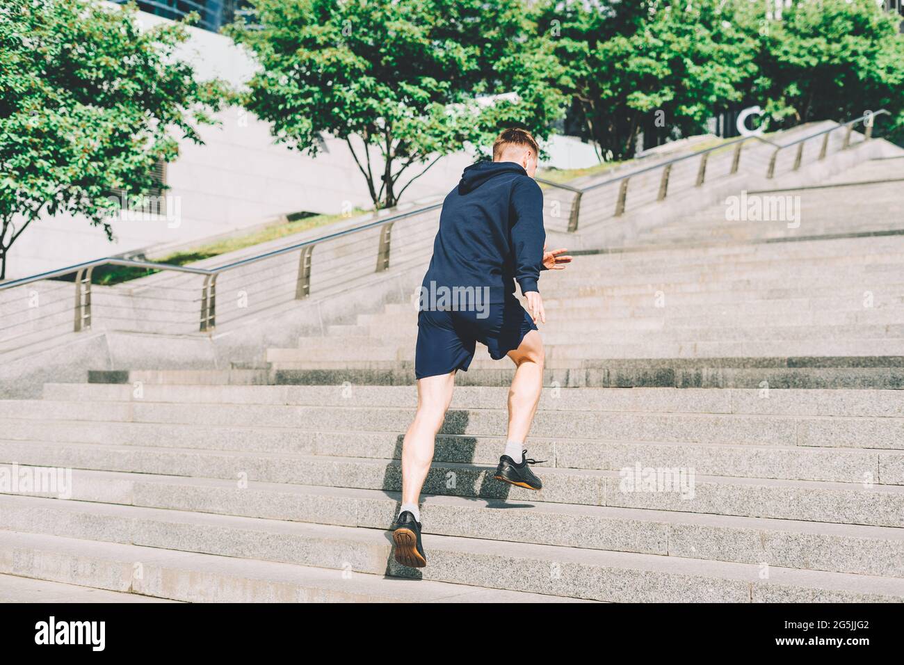 Young athlete man runner running up stairs on city stairs in summer on ...