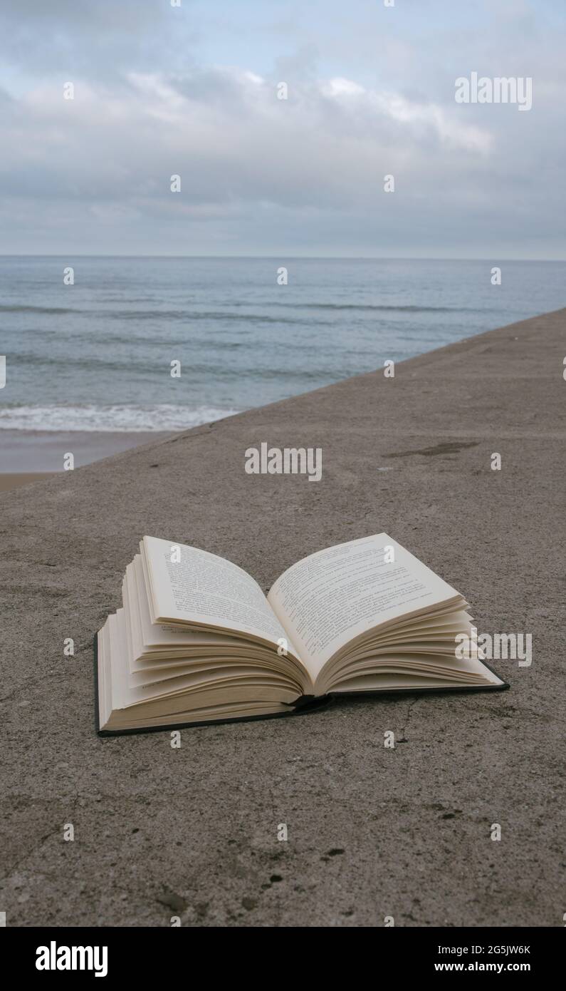 Open book on the ground with the cloudy sky and sea on the background ...