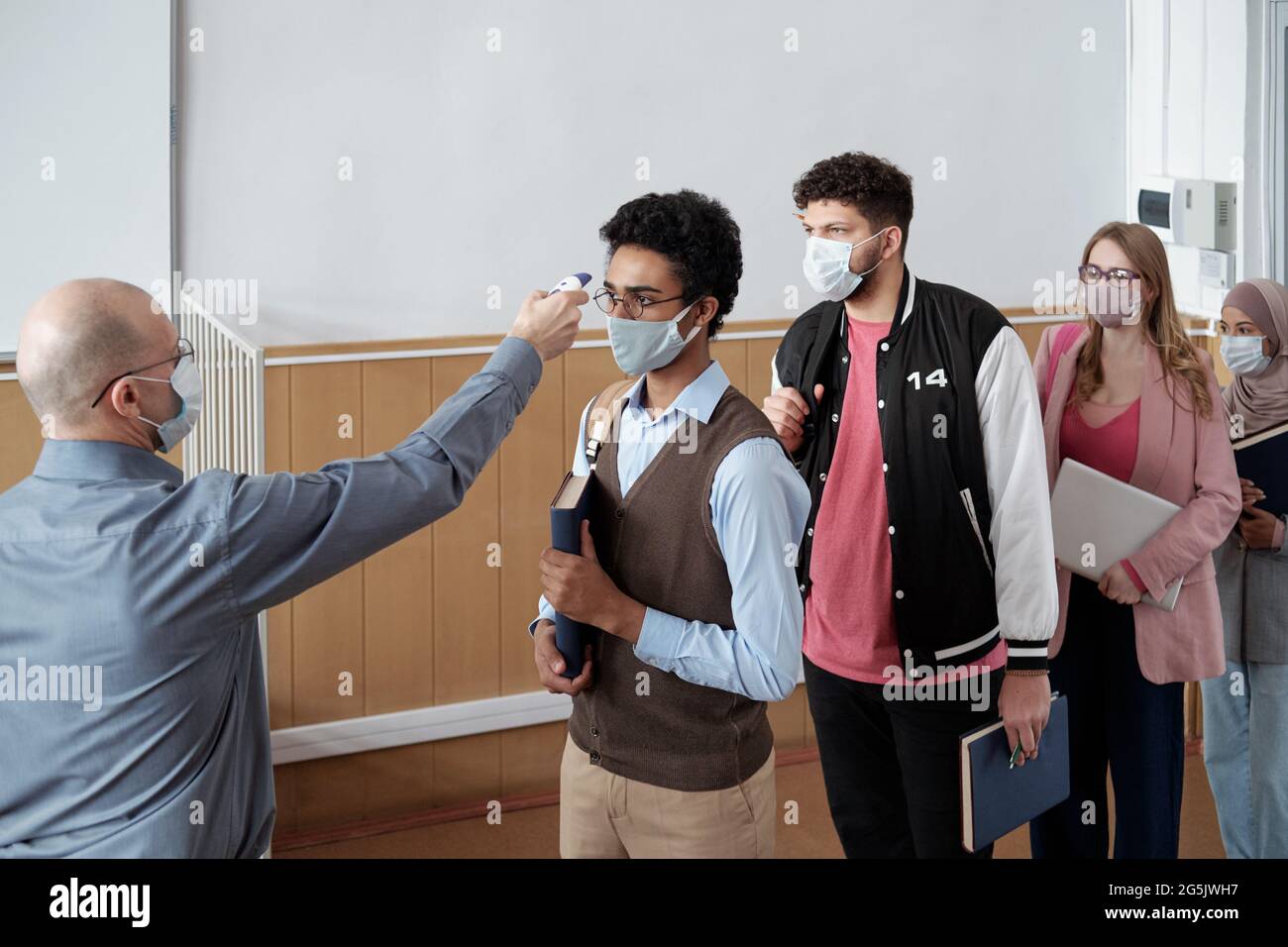 Mature professor measuring temperature of students before lesson Stock ...