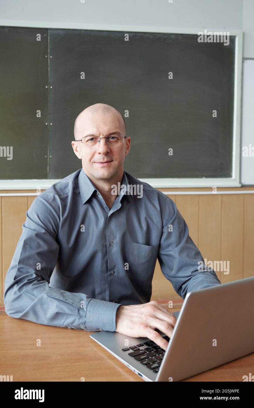 Successful male teacher sitting by workplace against blackboard Stock ...