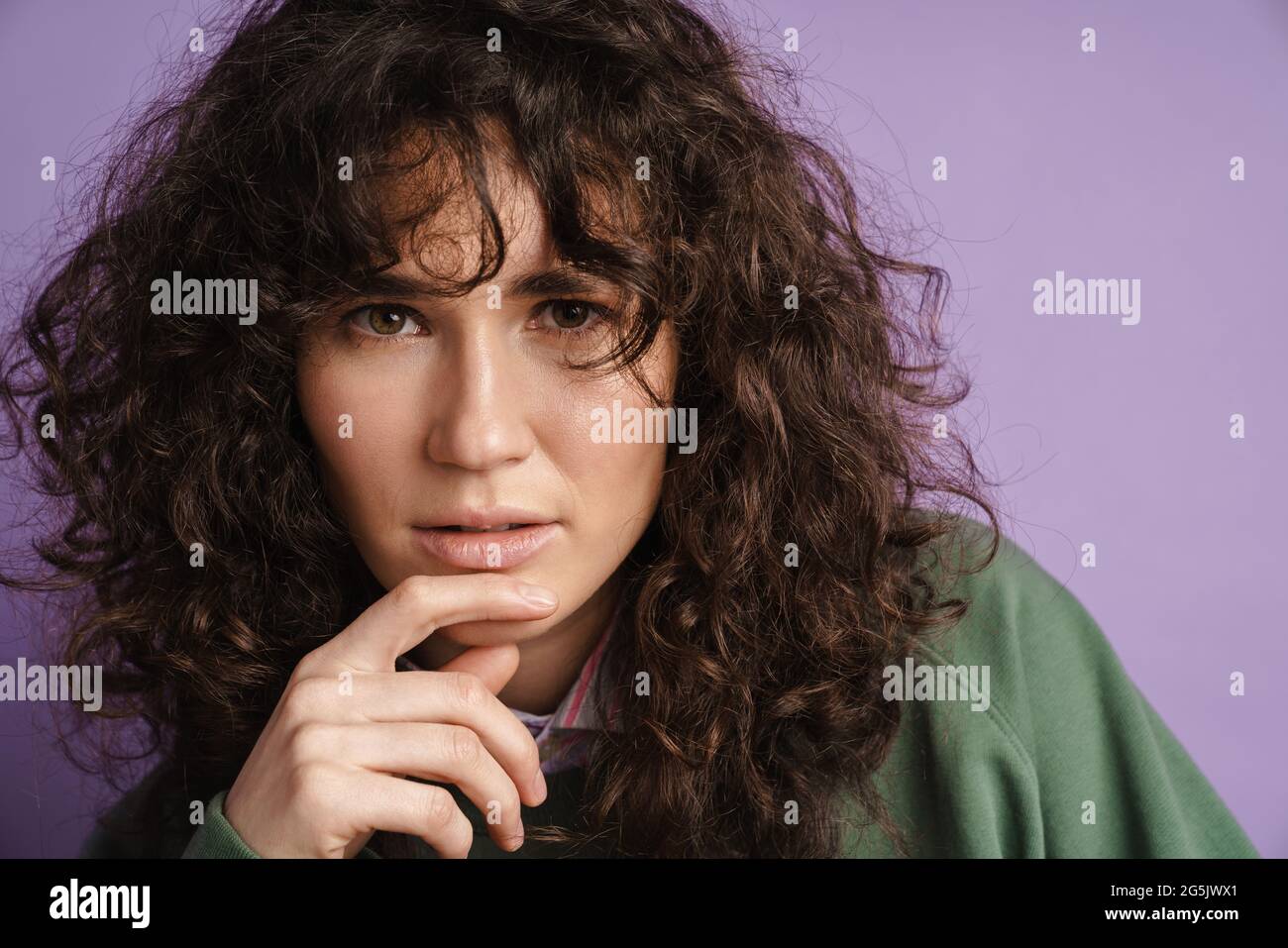 Brooding beautiful curly girl looking at camera with finger at her chin ...