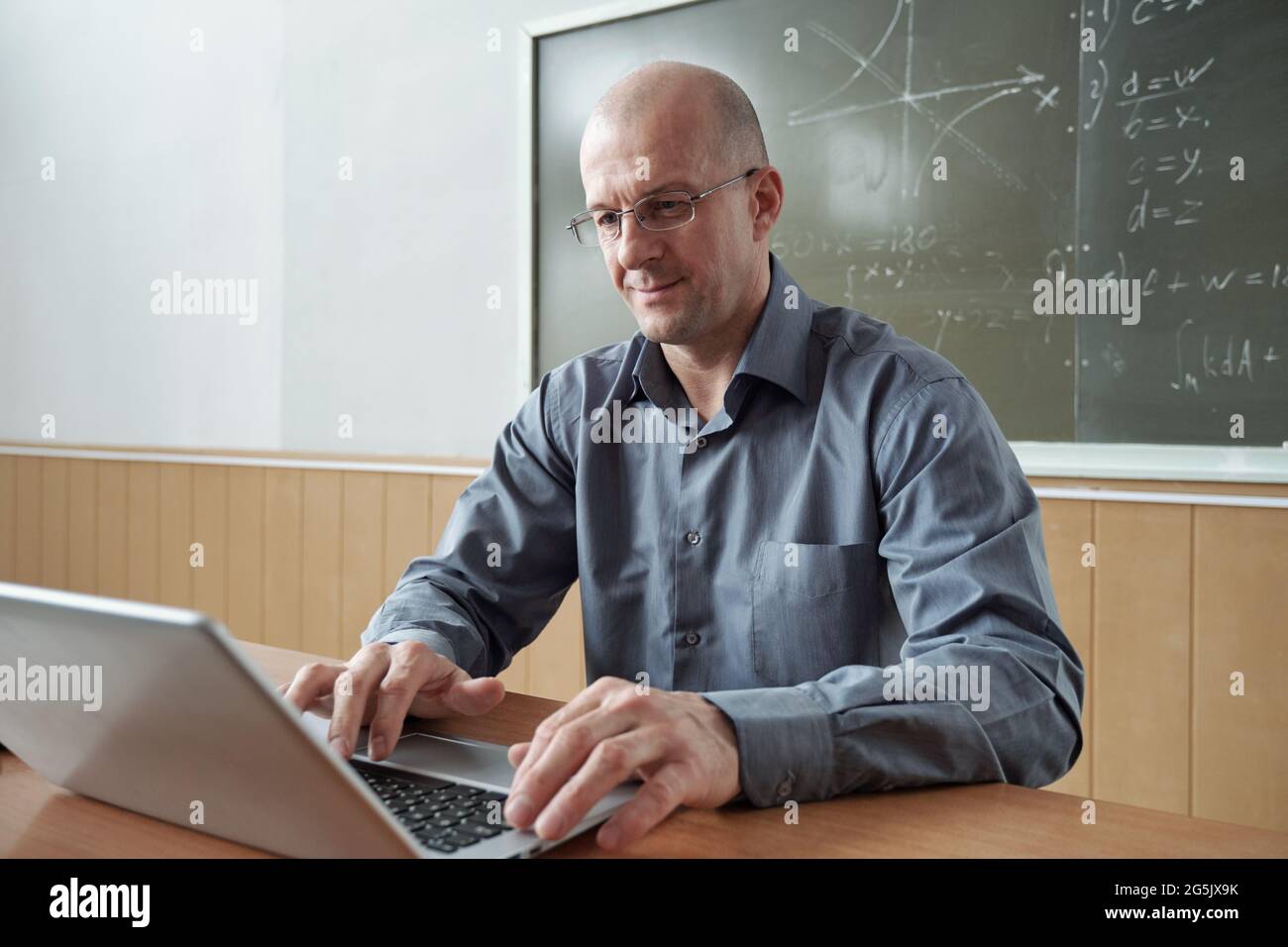 Contemporary teacher using laptop during online lesson in classroom ...