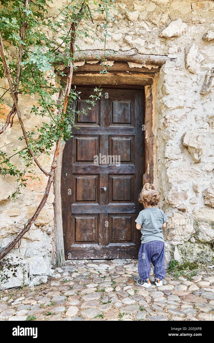 Back view of a lonely toddler standing outside in front of the closed ...