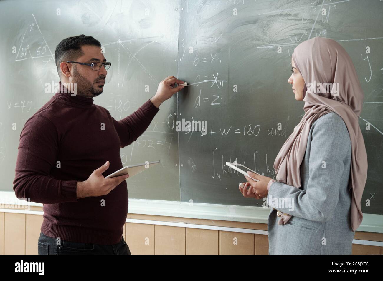 Teacher and student with tablets standing by blackboard at lesson of ...