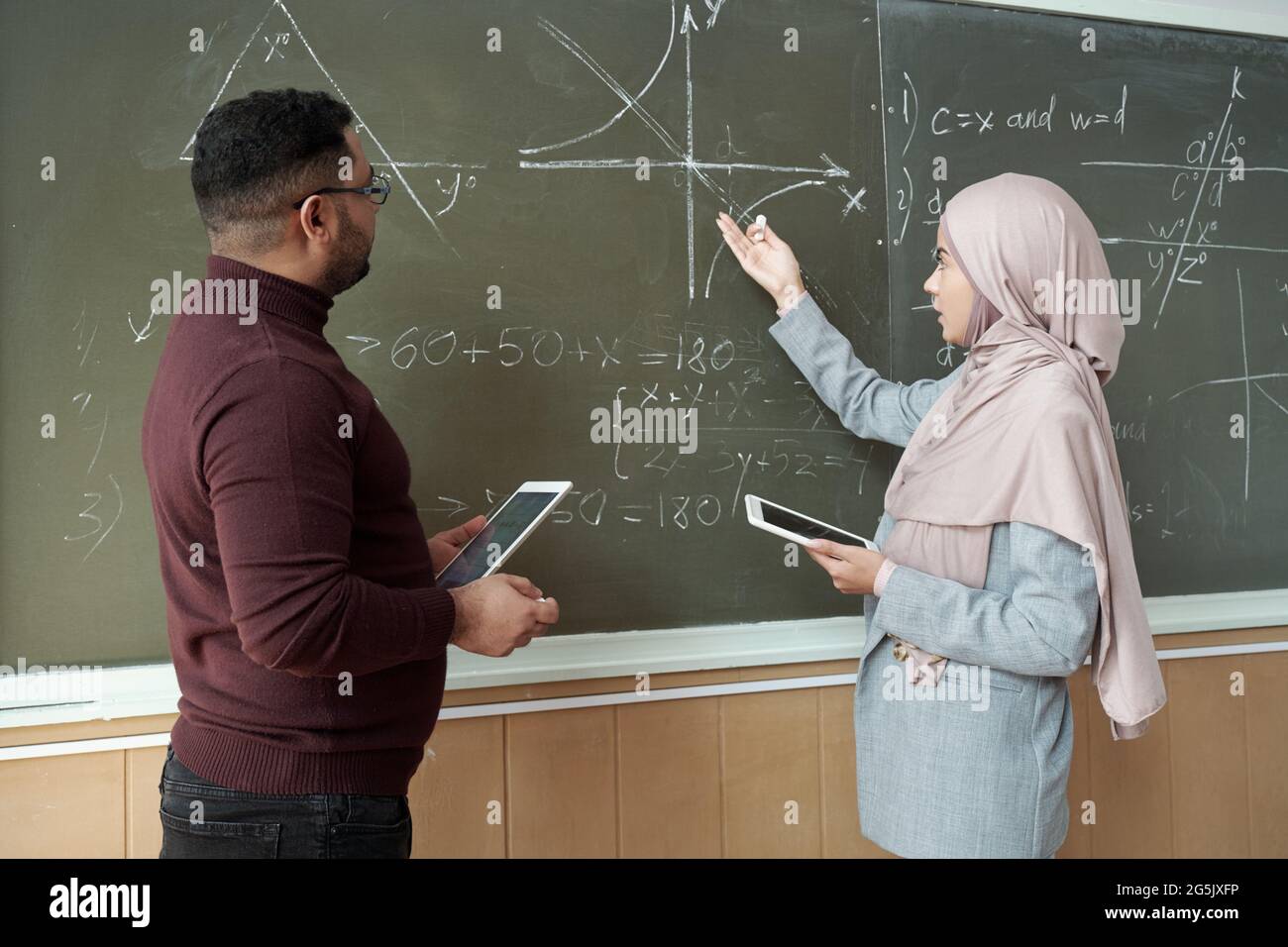 Young female student explaining graph to her teacher by blackboard ...
