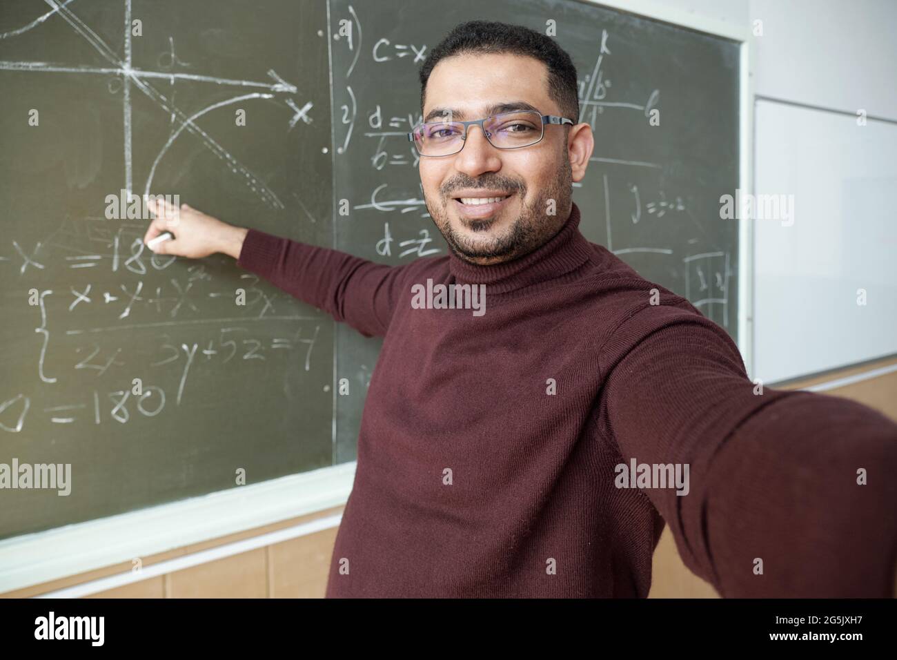 Successful teacher pointing at graph on blackboard during online lesson ...