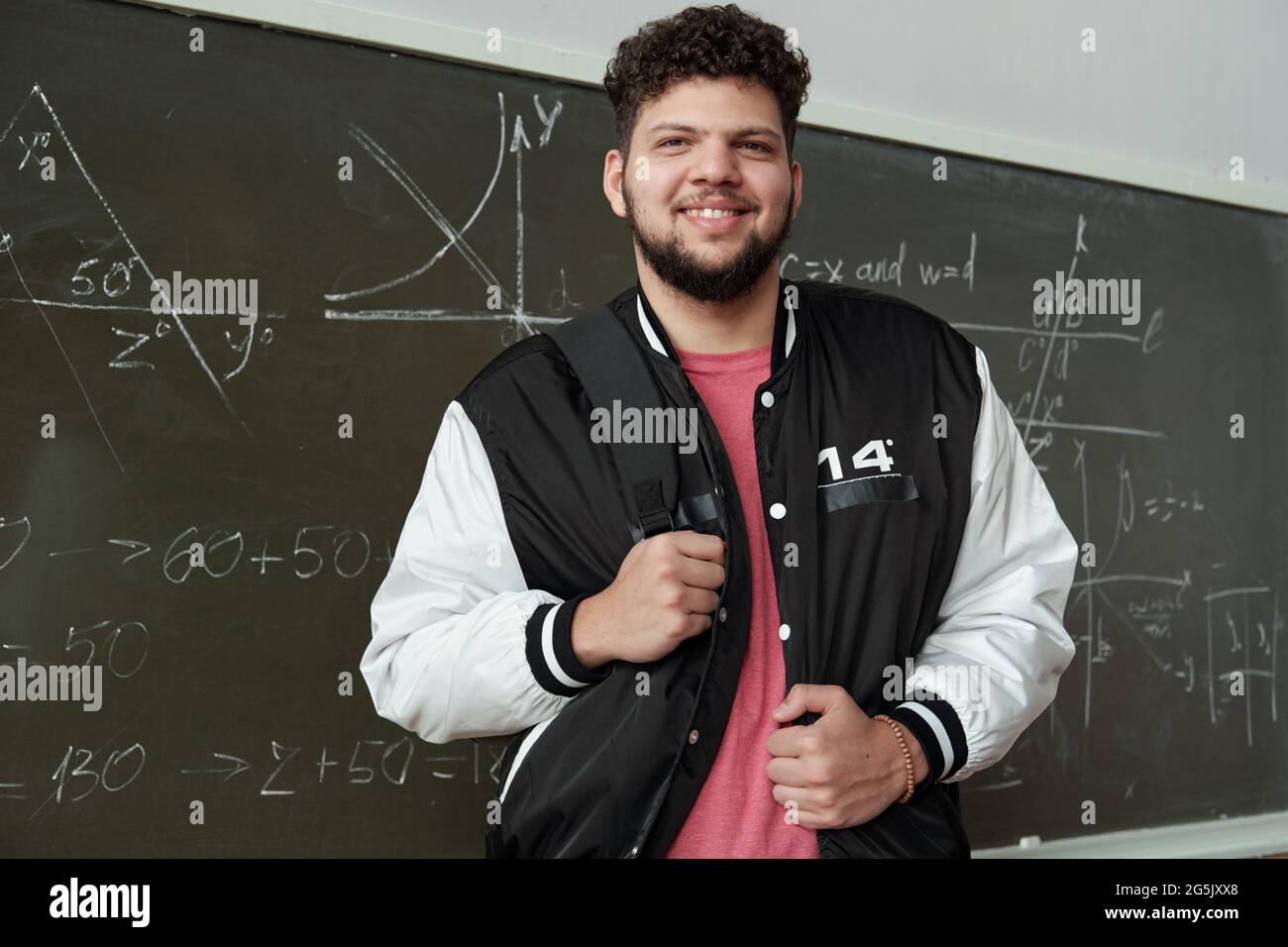 Happy student standing against blackboard in classroom Stock Photo - Alamy