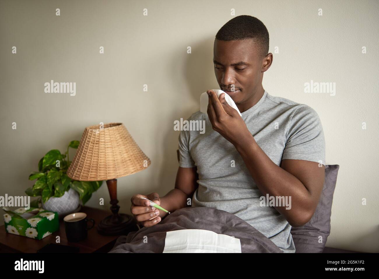 Young African man with a cold taking his temperature in bed Stock Photo ...