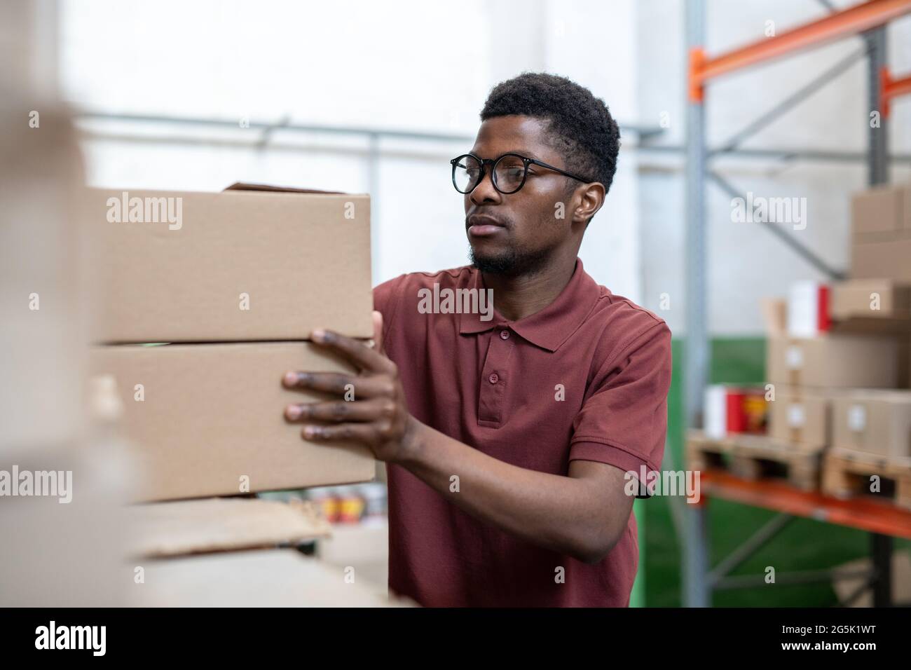 Young male worker of warehouse making stack of boxes with goods Stock ...