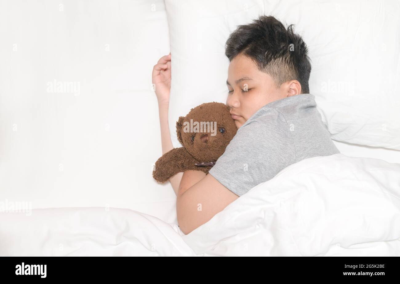 Obese fat boy is sleeping with a teddy bear in his bed at home, sweet ...