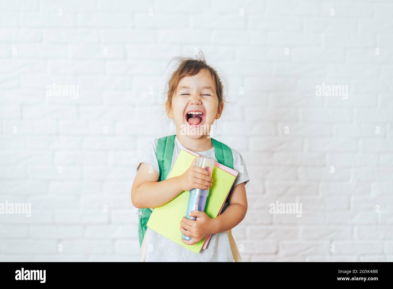 Child with green backpack holding school supplies Stock Photo - Alamy