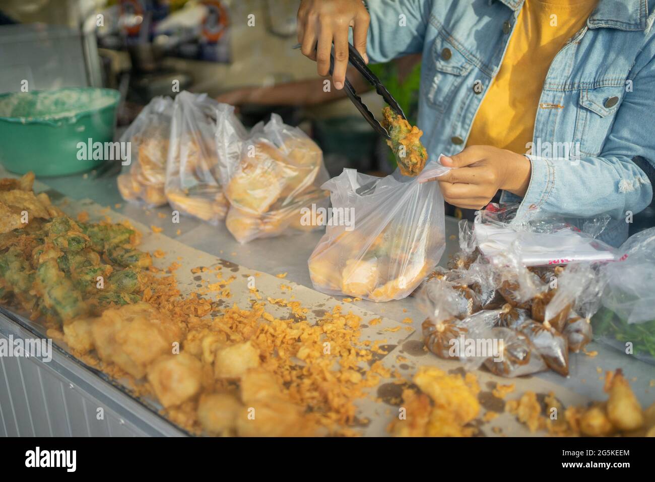 the seller uses tong tongs to take the fried food into a plastic ...