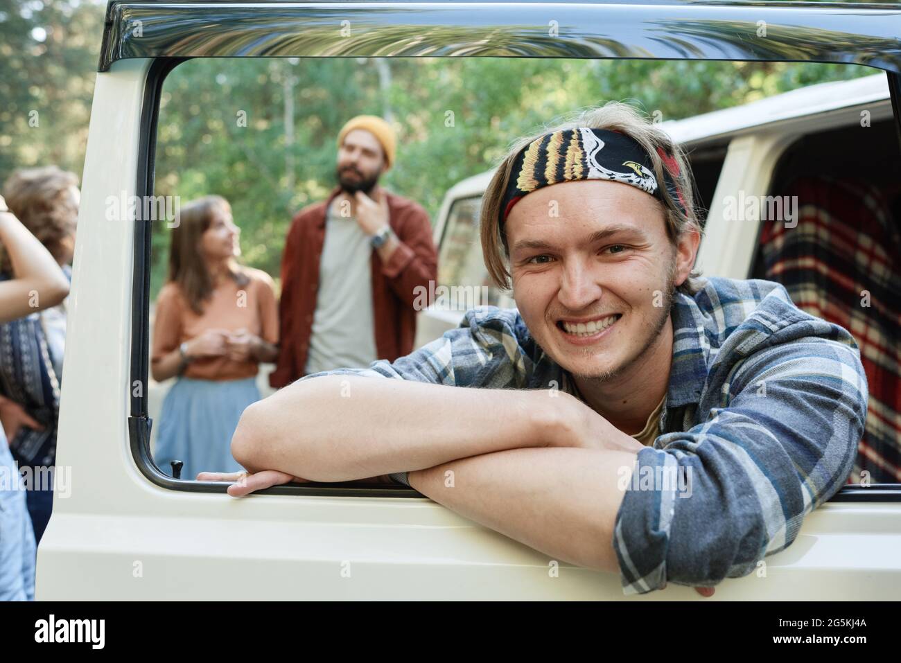 Portrait of guy smiling at camera sitting in the van with his friends ...