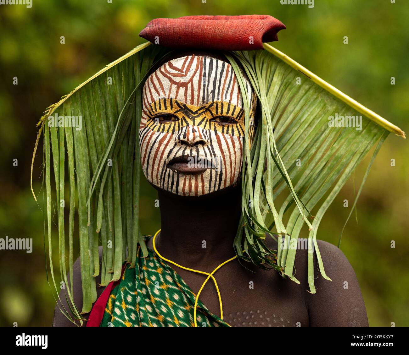 Palm leaves frame this Suri girl's intricately painted face. OMO VALLEY ...
