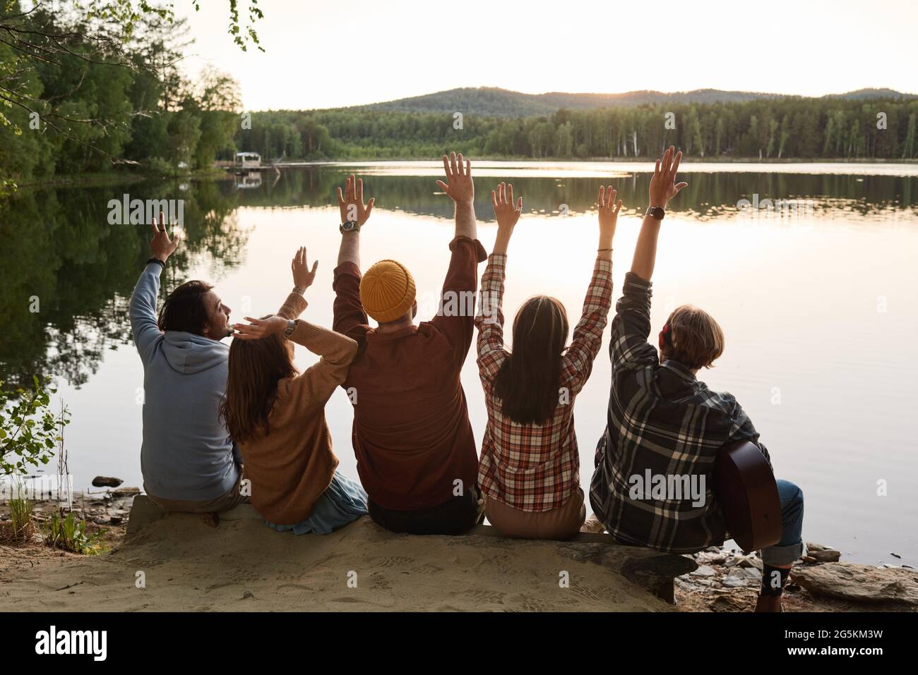 Rear view of group of friends raising their hands up while sitting on ...