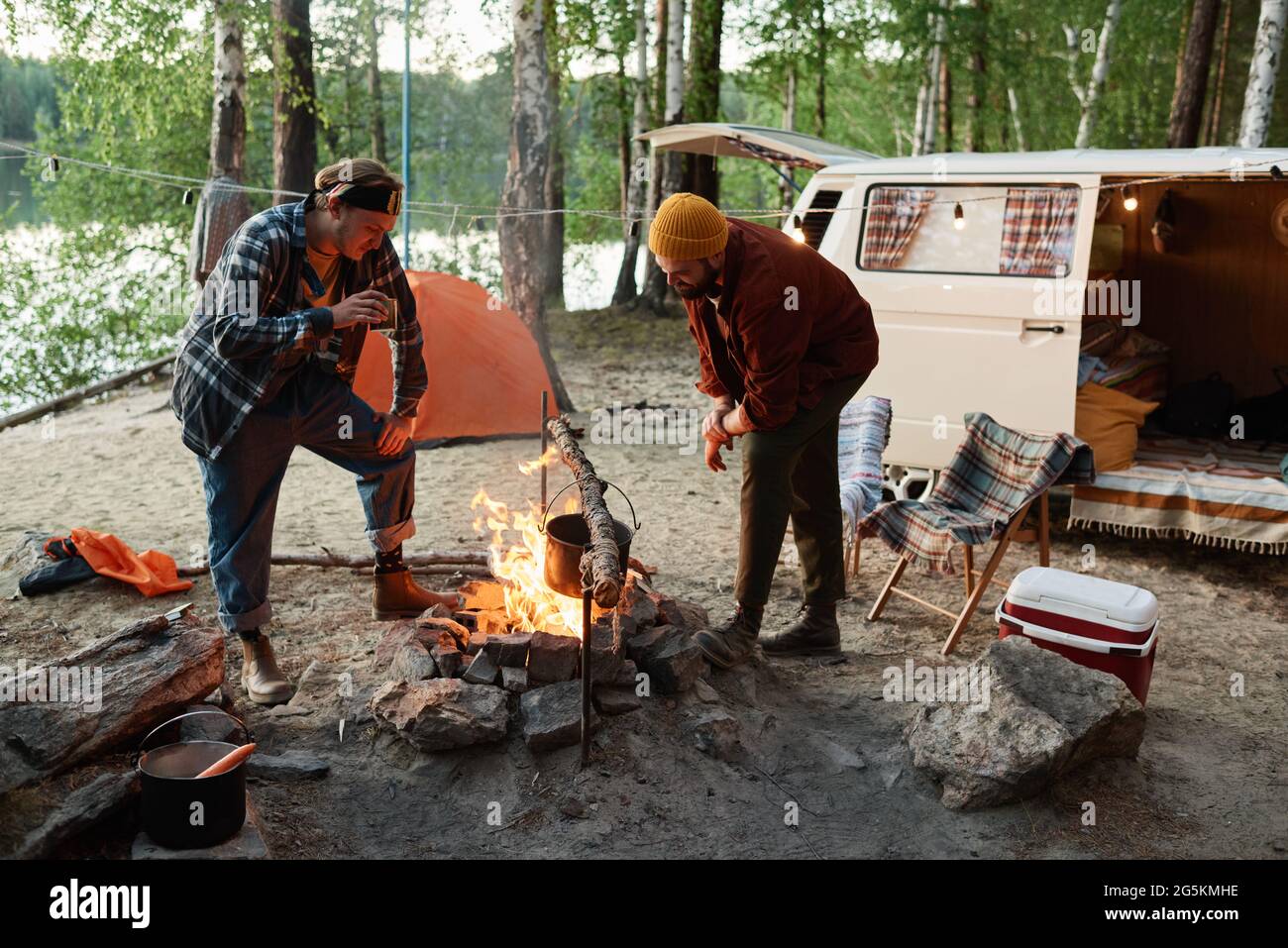 Two men cooking food together on a campfire during camping in the ...