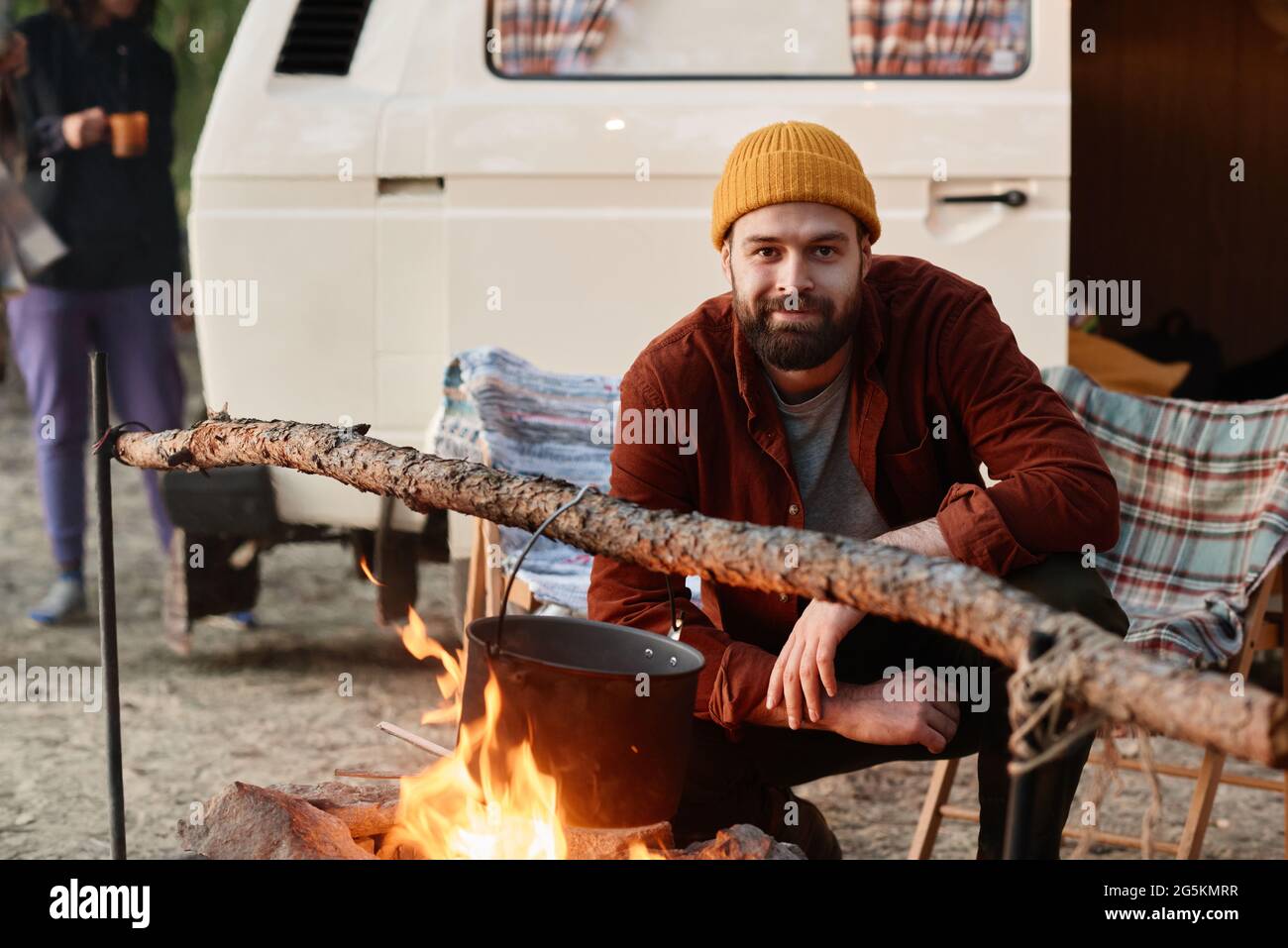 Portrait of young bearded man looking at camera while cooking food on a ...
