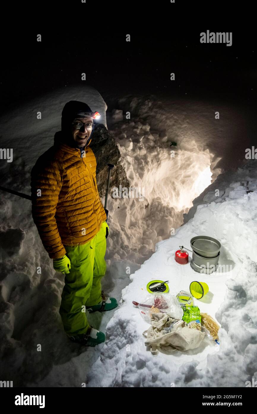Man cooking with a camping stove in front of a snow cave, camping in ...