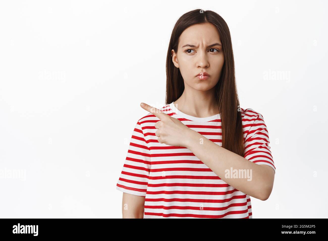 Suspicious girl squinting, pointing and looking left with doubtful ...