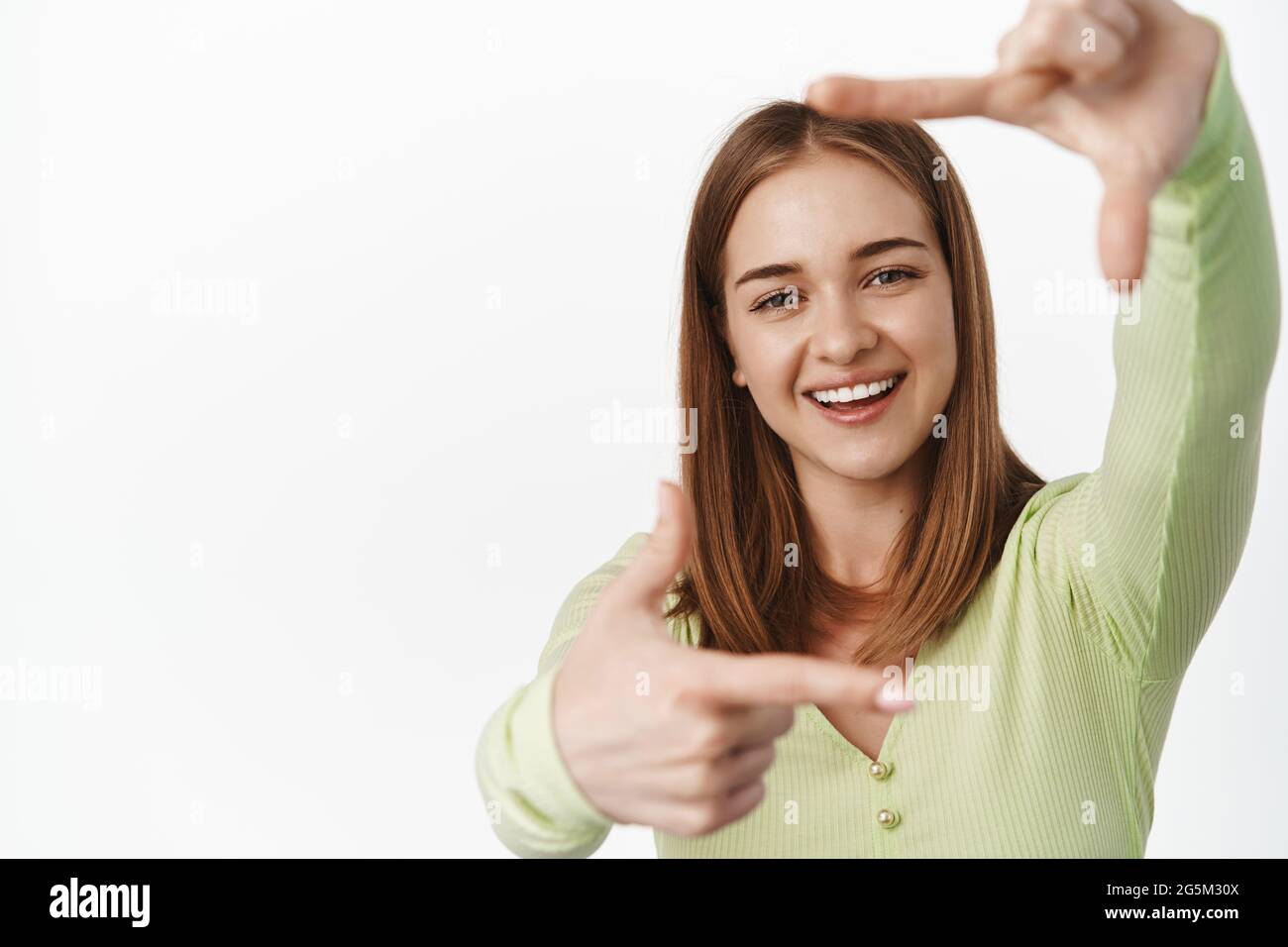 Portrait of smiling blond girl looks through finger frames creative ...