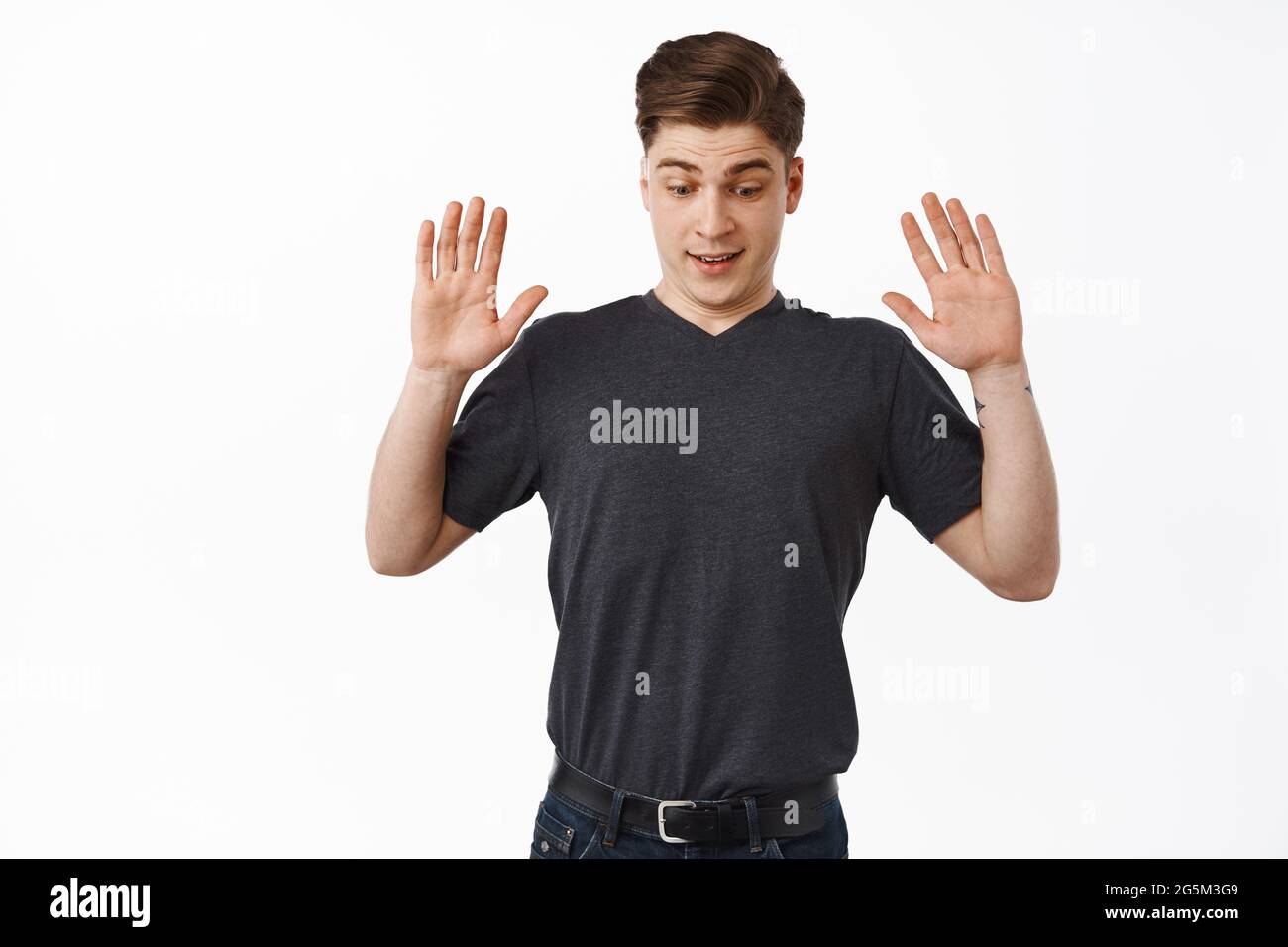 Surprised young man drop something, raising hands up and looks down ...