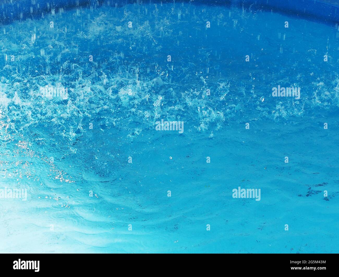 Fragment of blue pool with splashes of water from a pouring fountain ...