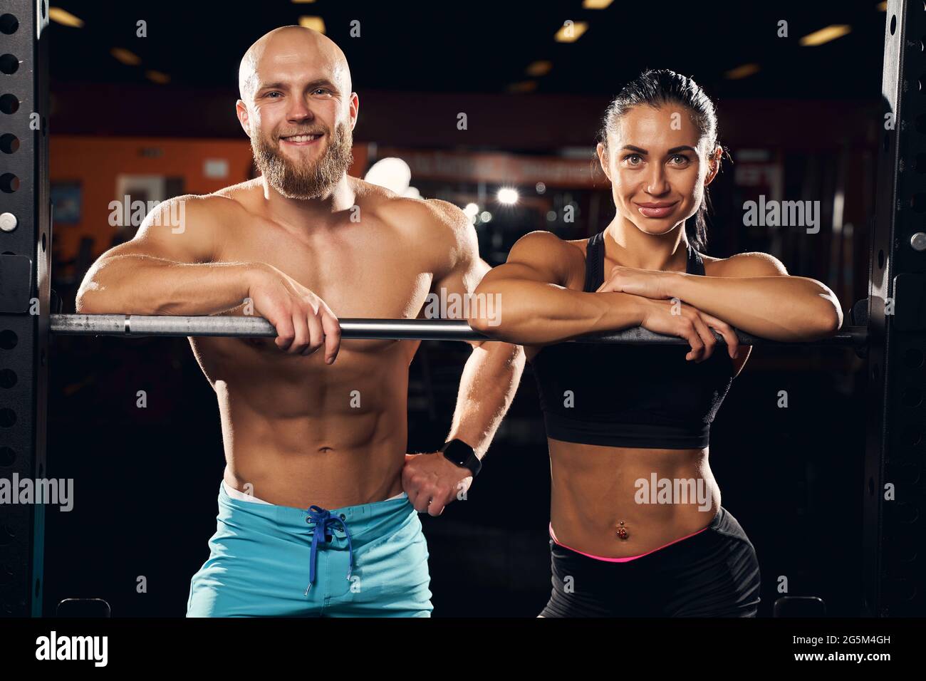 Two workout buddies posing next to a barbell Stock Photo - Alamy