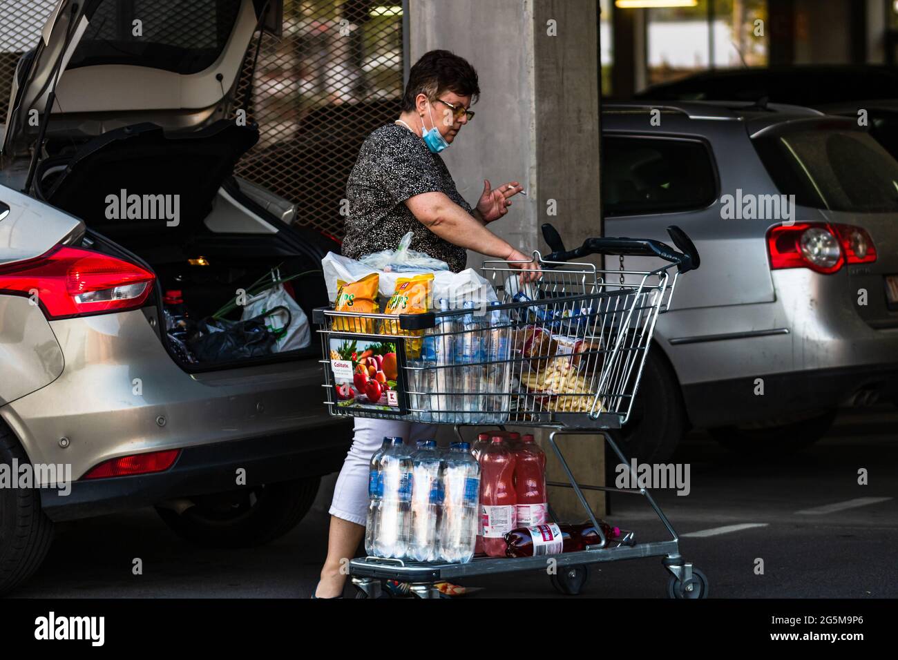 Woman wearing surgical mask with shopping cart full of goods, putting ...