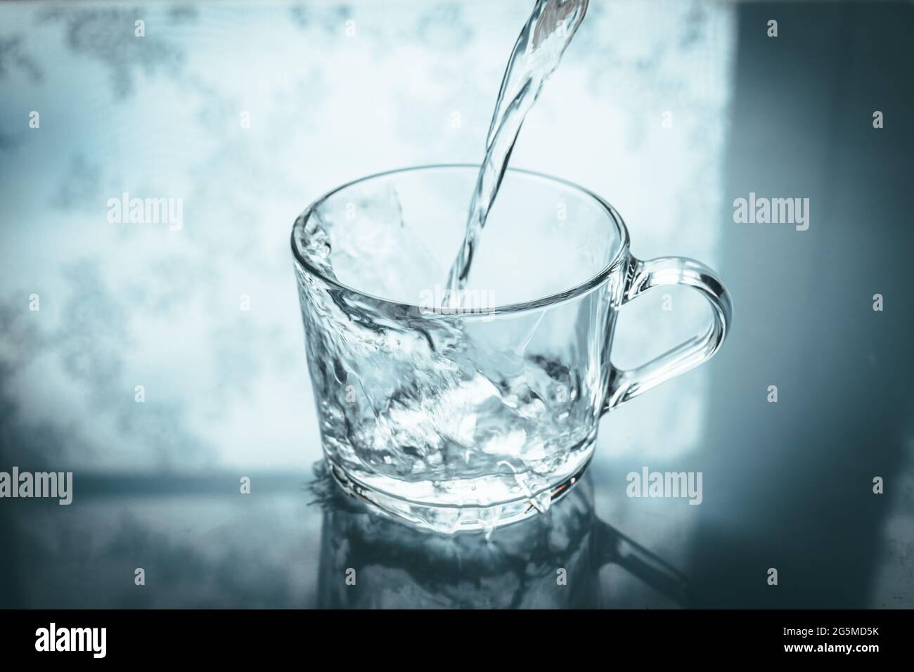 Pouring water into a glass, blue pastel background Stock Photo - Alamy