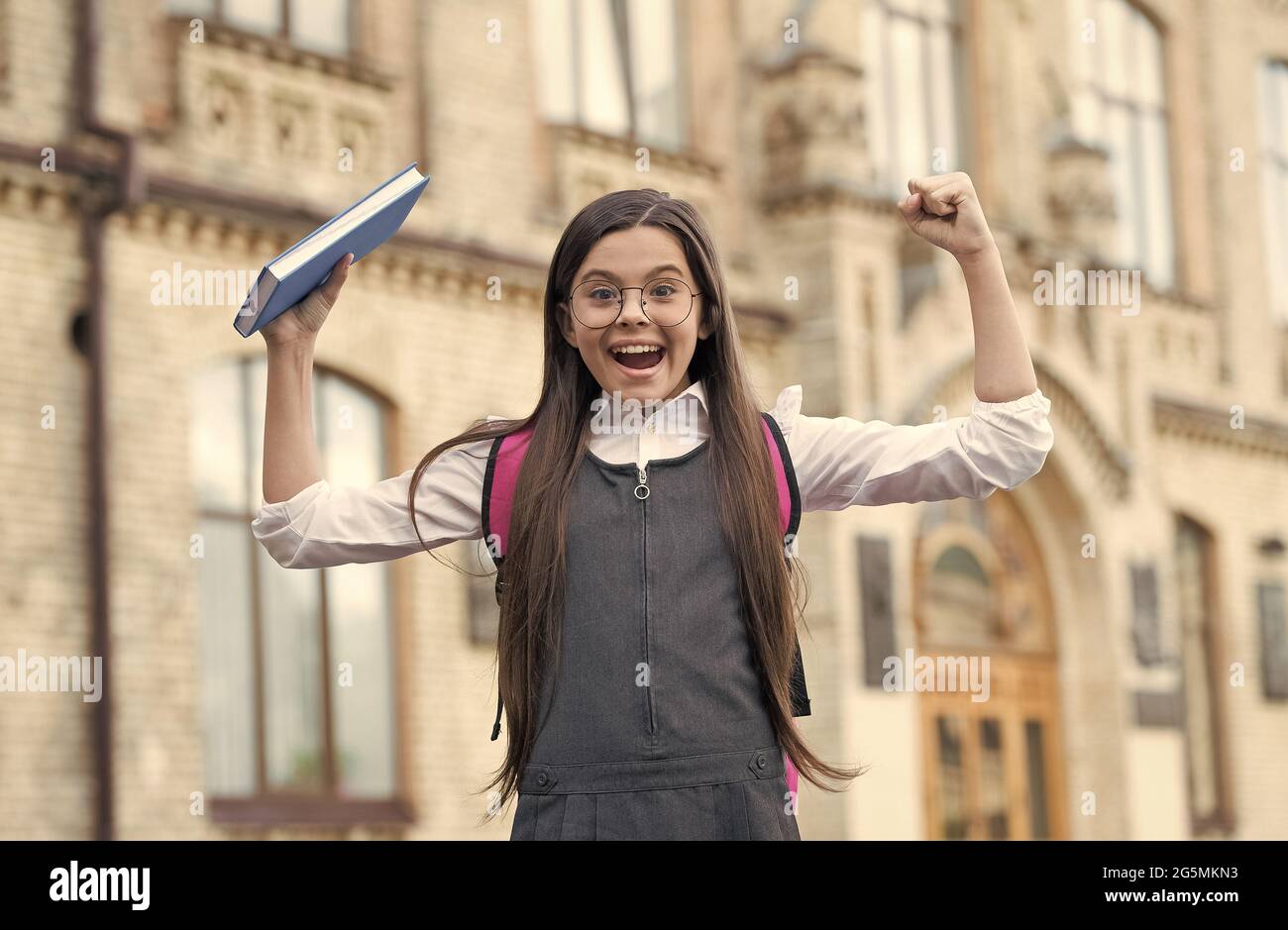 Happy kid show power hand gesture holding school book outdoors ...