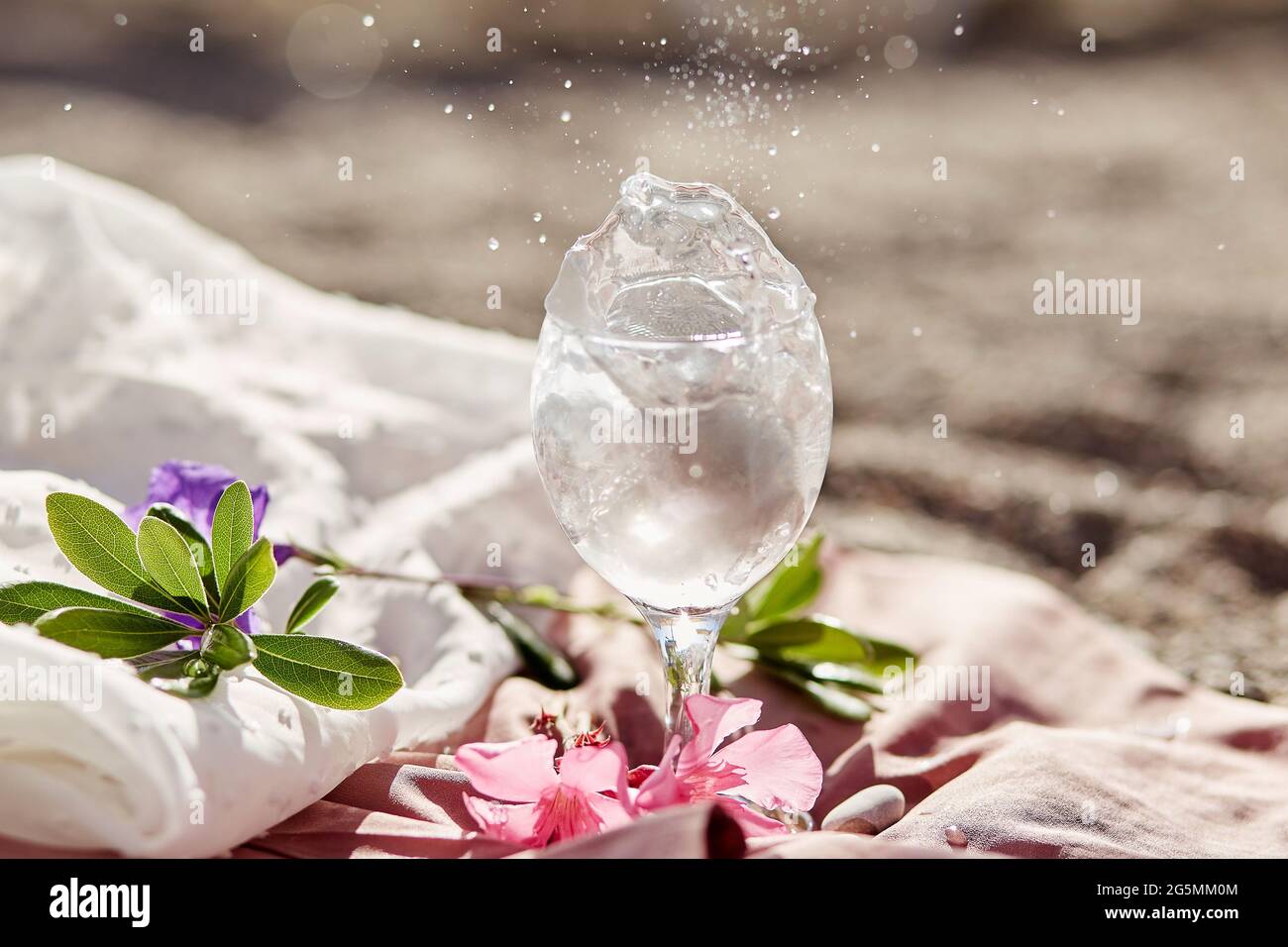 Explosion of tonic cocktail in wine glass on beach with flowers. Summer cocktail. Delicate silk ...