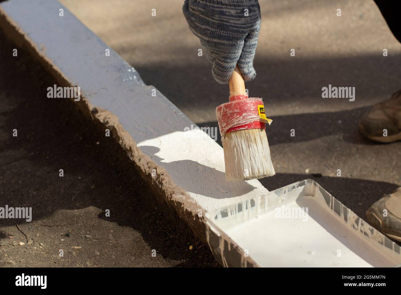 Paints the kerb with white paint. Brush with paint for the road curb ...