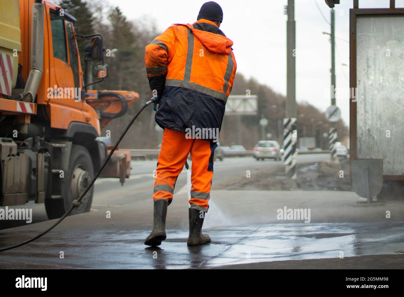 Sanitary handling of the bus stop. A man washes the road with a jet of ...