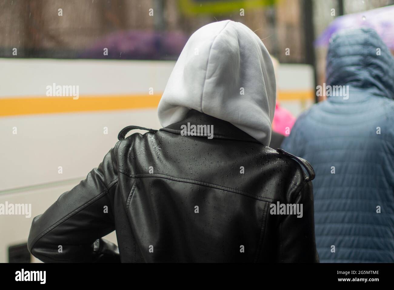 People from the back in the rain. Hooded people walk towards the bus ...