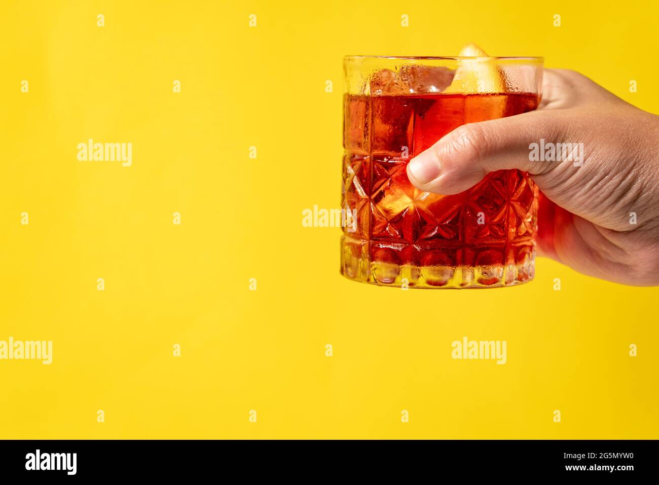 Close up view of negroni drink being hand held with yellow background ...