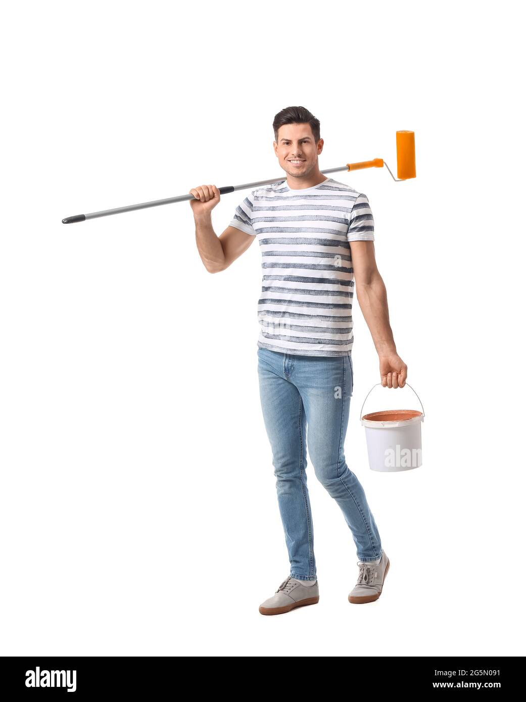 Young man with paint roller and bucket of paint on white background ...