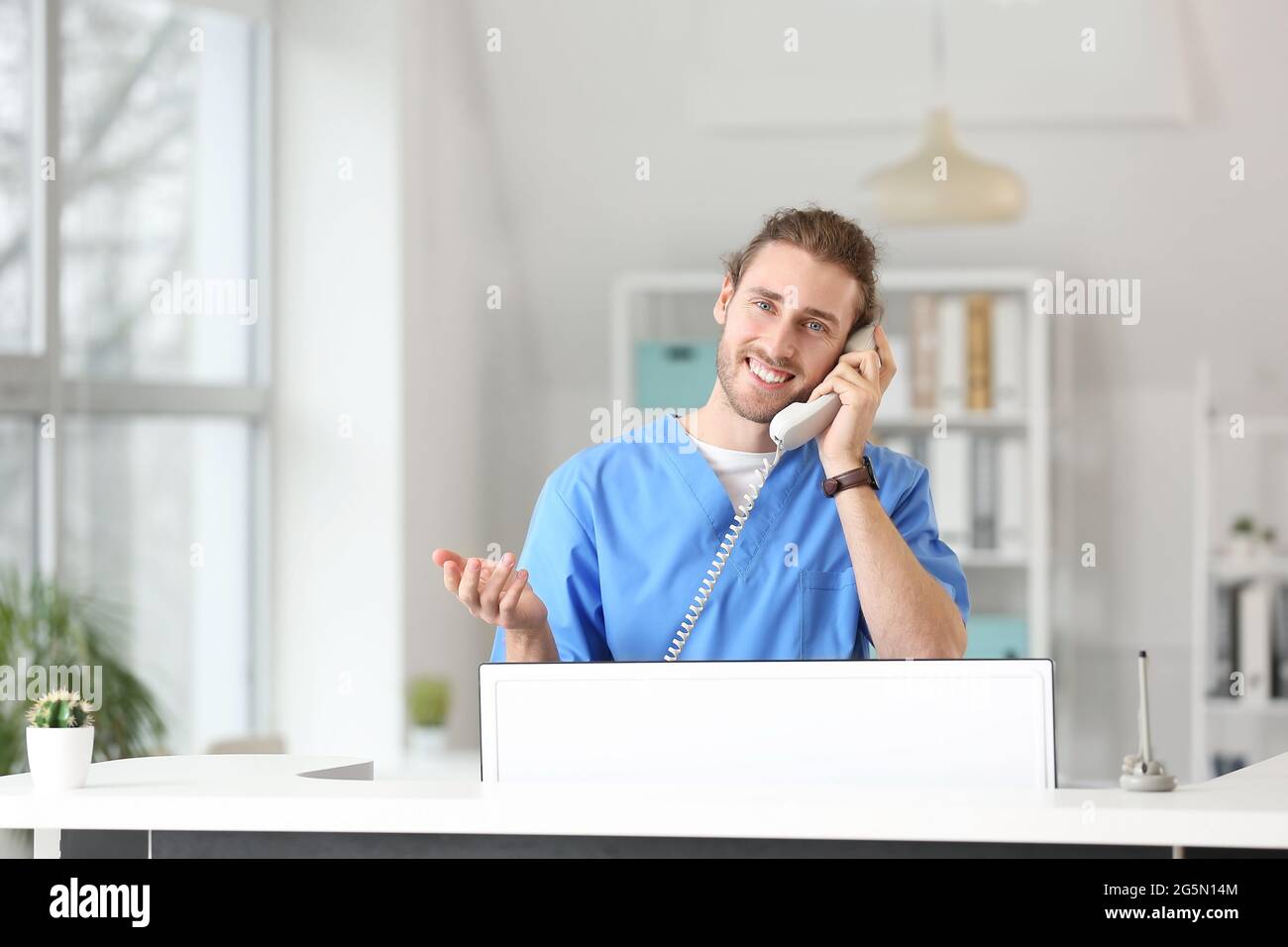 Young receptionist talking by telephone in clinic Stock Photo - Alamy